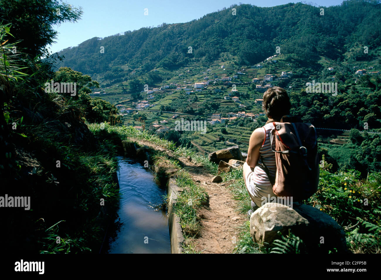 Woman with rucksack sitting looking over man made water channel and ...