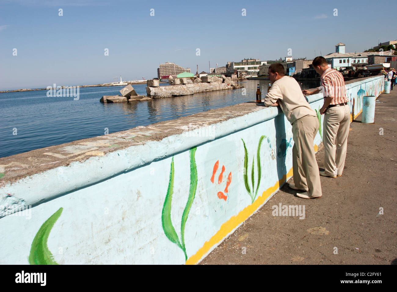 Two men drink beer by a colourful wall on the waterfront in Kholmsk ...