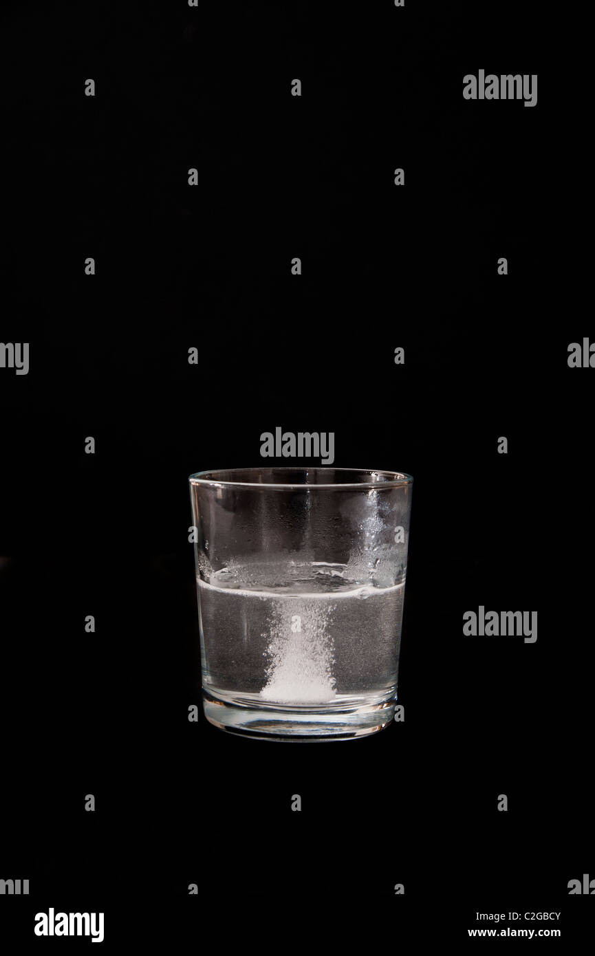 An effervescent tablet dispersing and dissolving in a glass of water ...