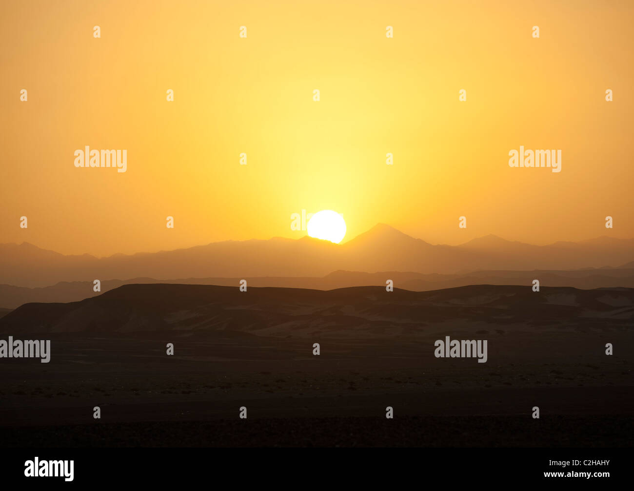 Sun setting in the desert over distant mountains Stock Photo - Alamy