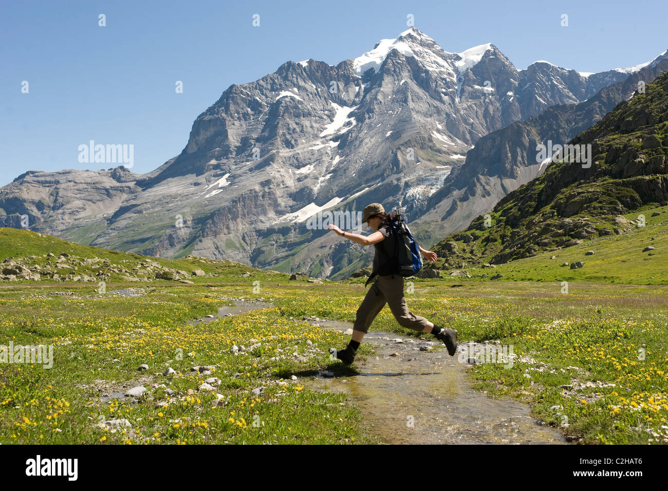 A woman jumping over a mountain stream, Lauterbrunnental, Switzerland ...