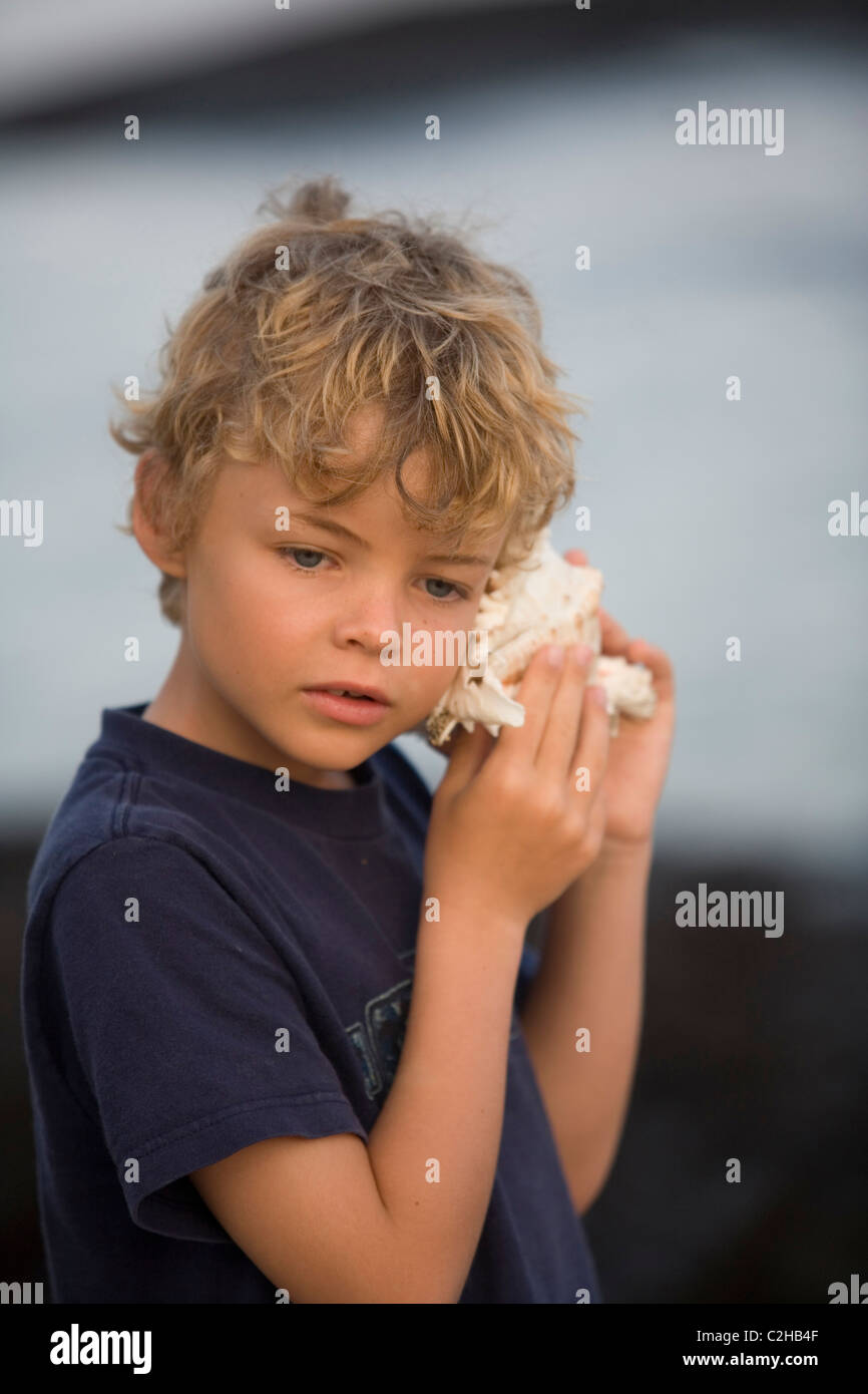 Young boy holding a conch shell up to his ear Stock Photo - Alamy