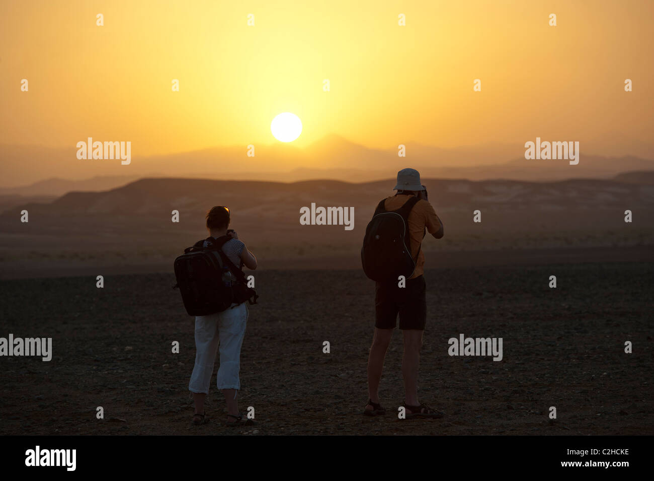 Two people in the desert photographing the sunset over mountains Stock ...