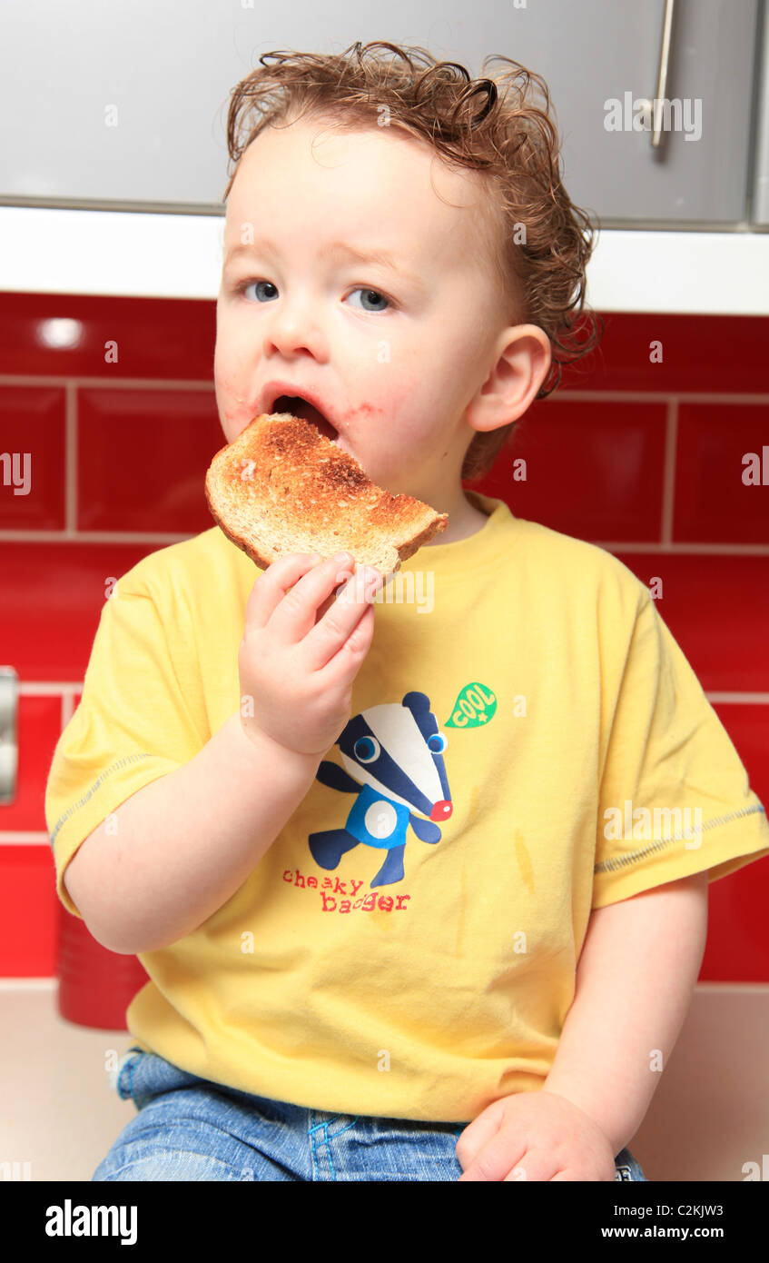 Toddler boy sitting on kitchen counter eating toast Stock Photo - Alamy
