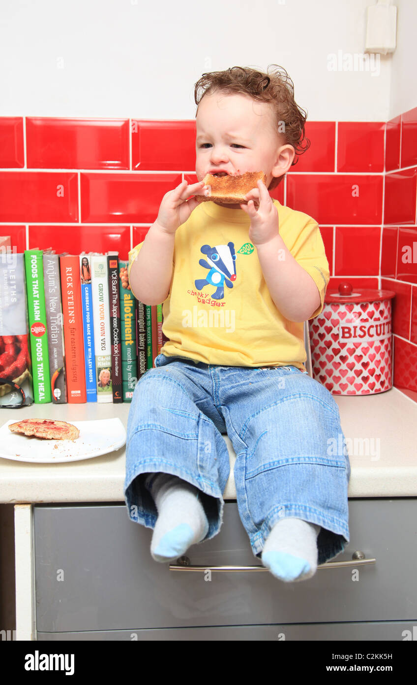 Toddler boy sitting on kitchen counter eating toast Stock Photo - Alamy