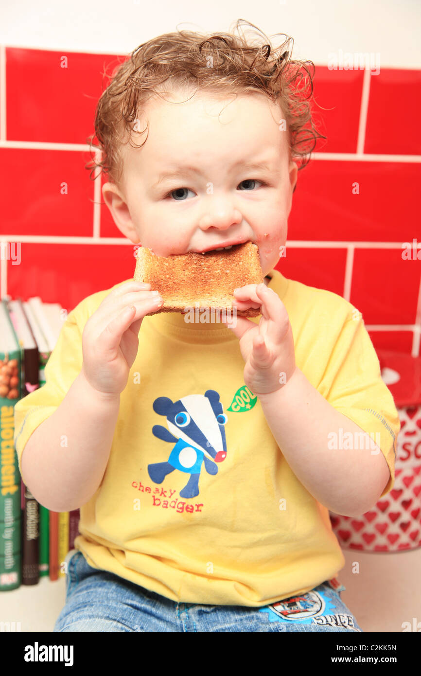 Toddler boy sitting on kitchen counter eating toast Stock Photo - Alamy