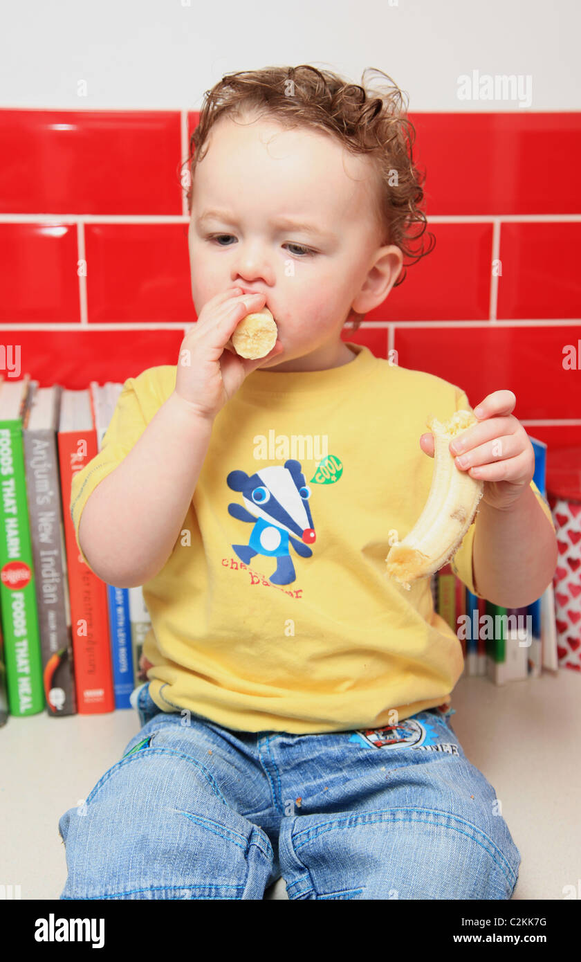Toddler boy sitting on kitchen counter eating toast Stock Photo - Alamy