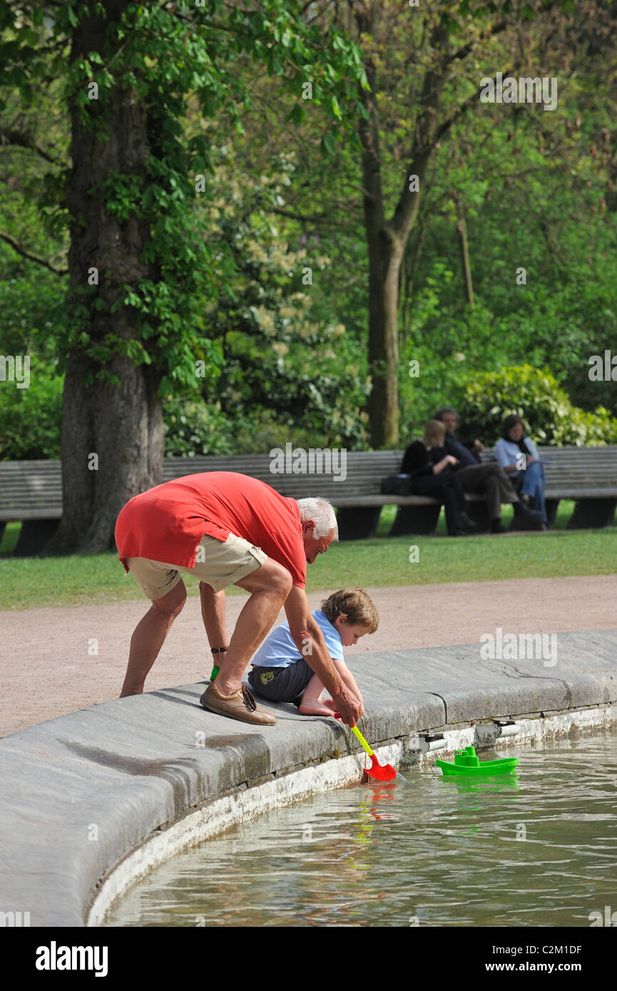 Grandfather surveilling child playing with plastic boat in water of ...