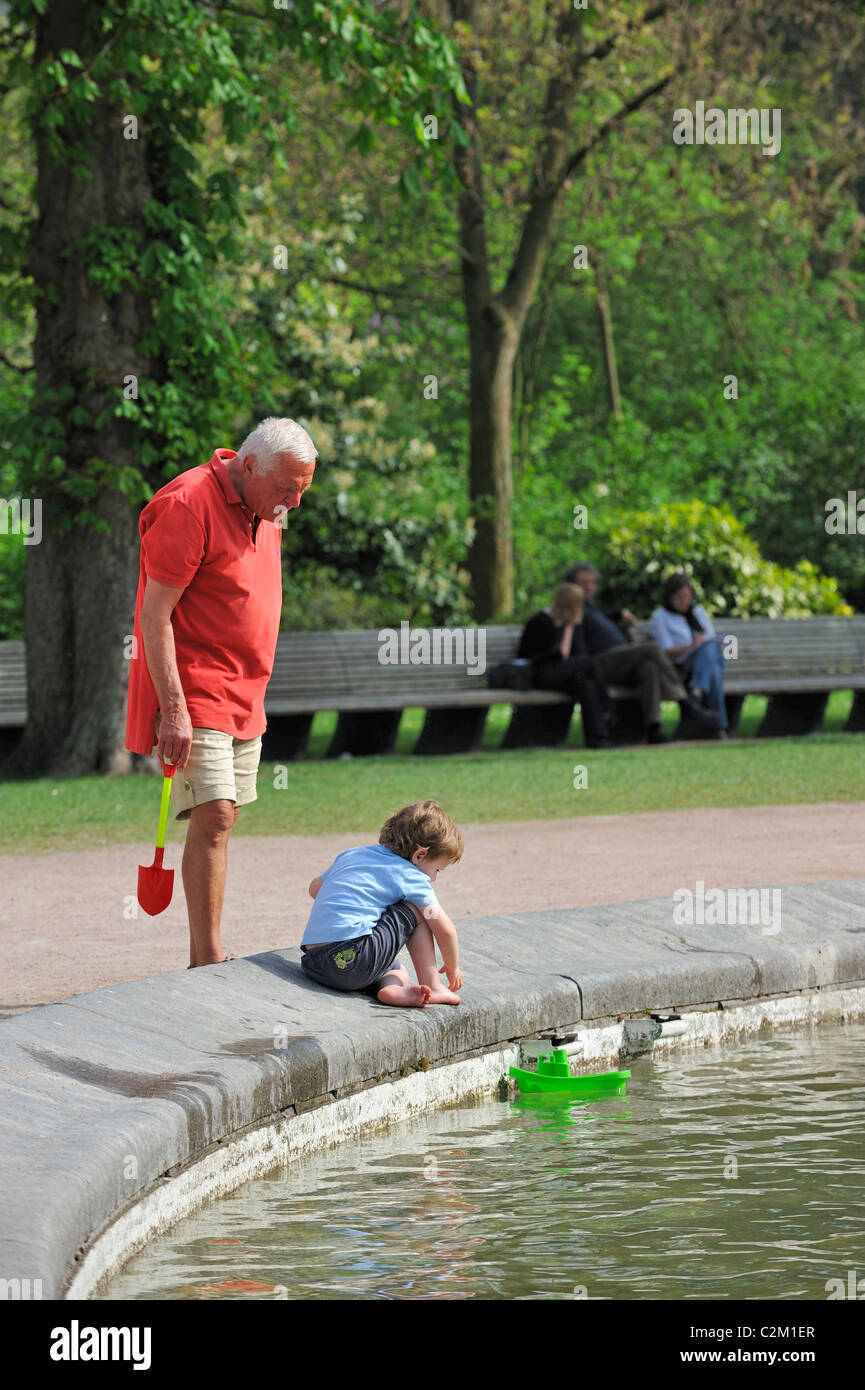 Grandfather surveilling child playing with plastic boat in water of ...