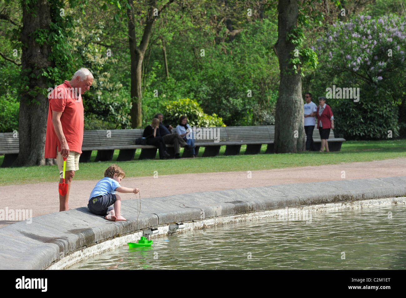 Grandfather surveilling child playing with plastic boat in water of ...