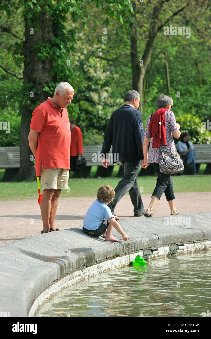 Grandfather surveilling child playing with plastic boat in water of ...