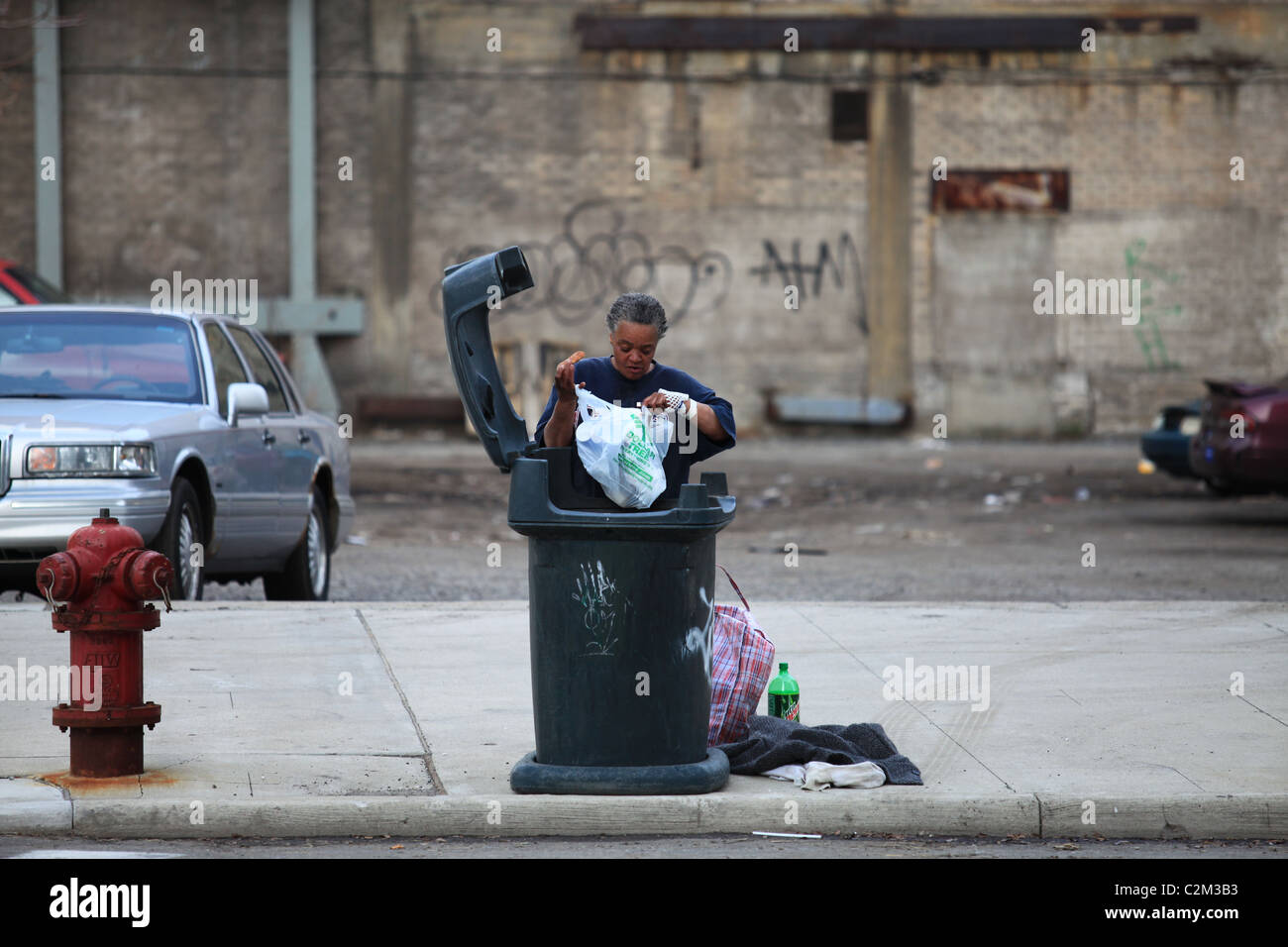 Hungry homeless black woman searching garbage for foods in downtown ...