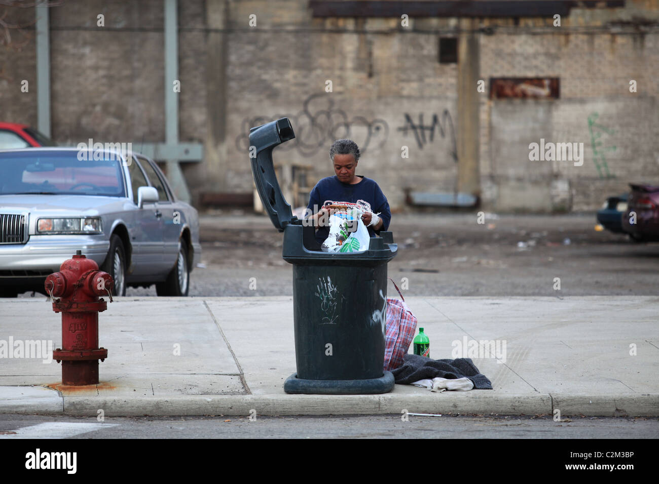 Hungry homeless black woman searching garbage for foods in downtown ...