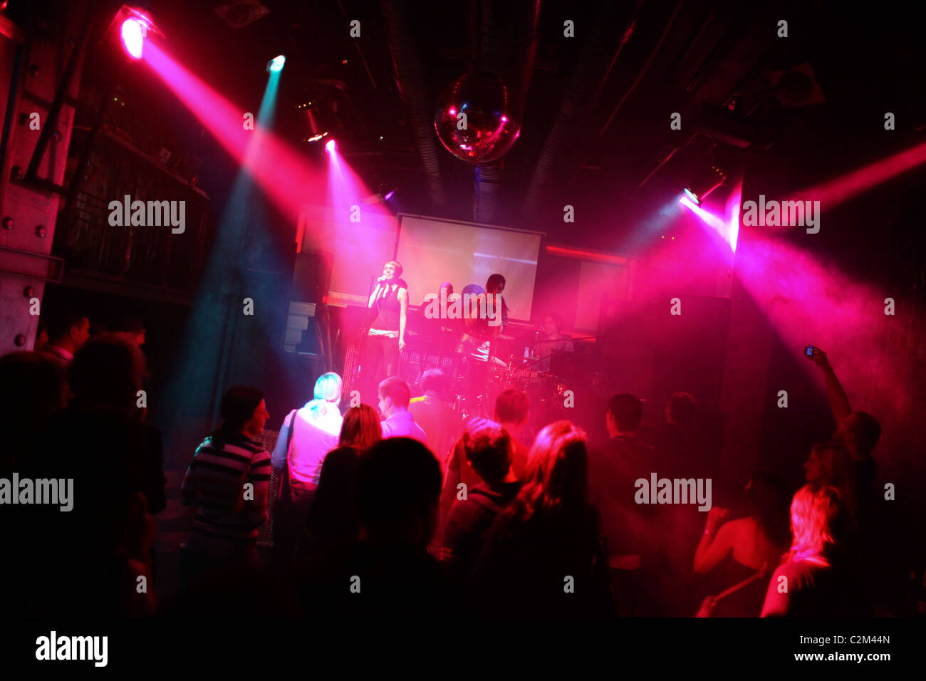 A crowd of people watching live music performance lit with spotlights ...