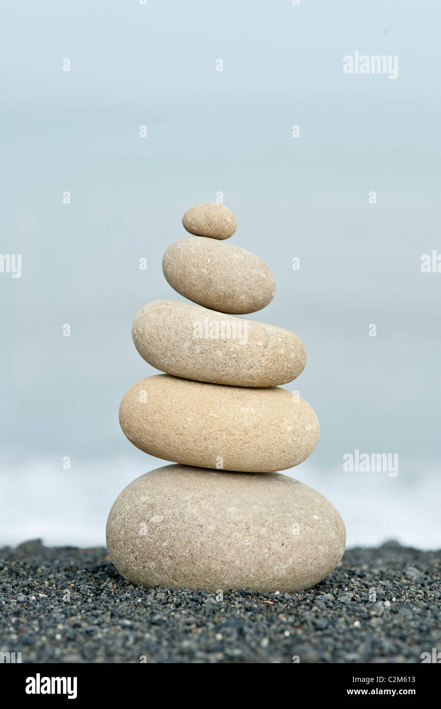 pile of balanced rocks on black sand beach with ocean waves background ...