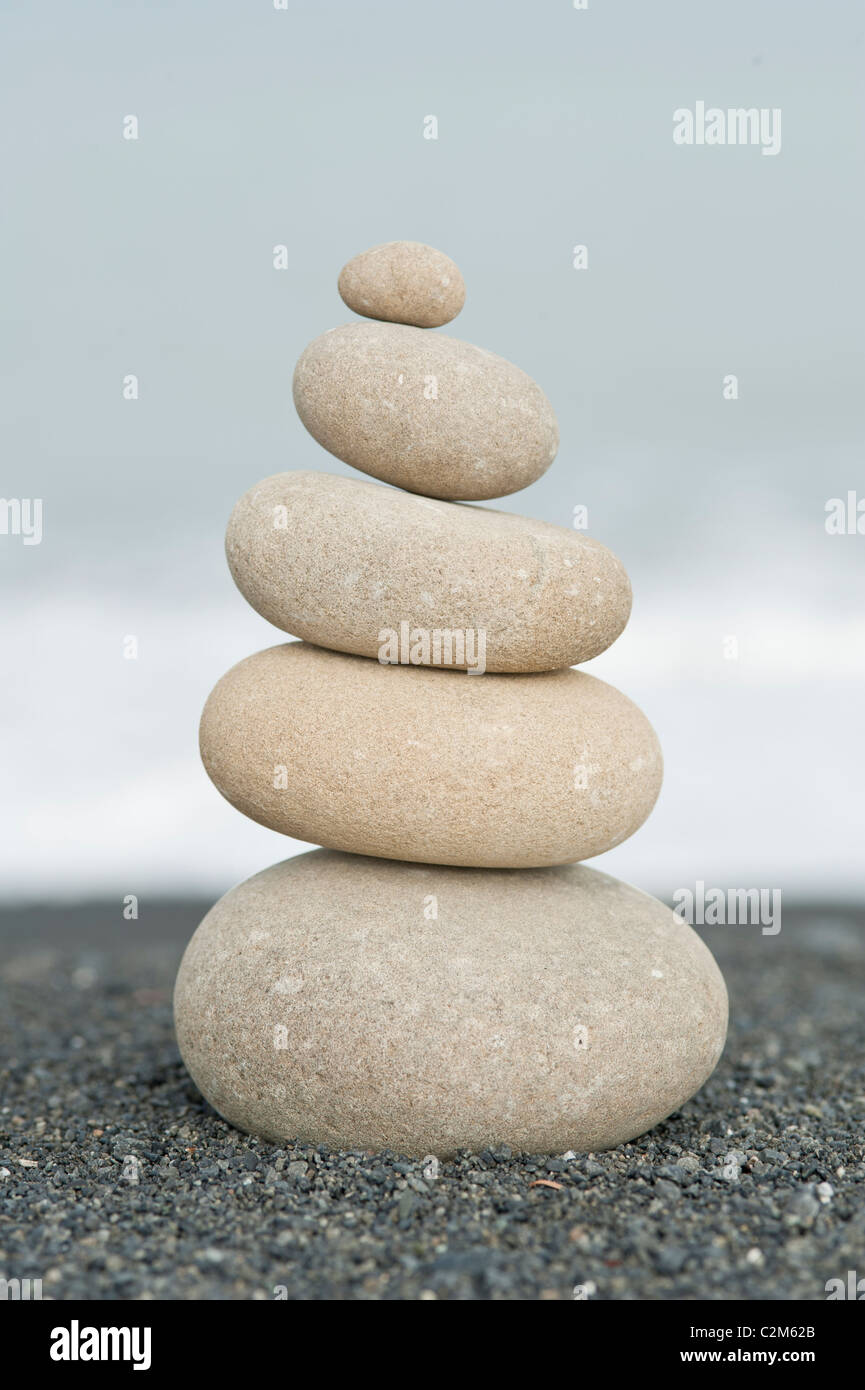 pile of balanced rocks on black sand beach with ocean waves background ...
