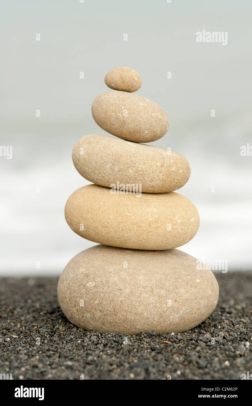 pile of balanced rocks on black sand beach with ocean waves background ...