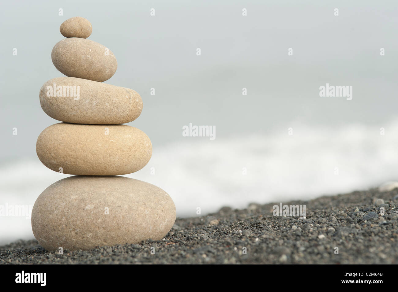 pile of balanced rocks on black sand beach with ocean waves background ...