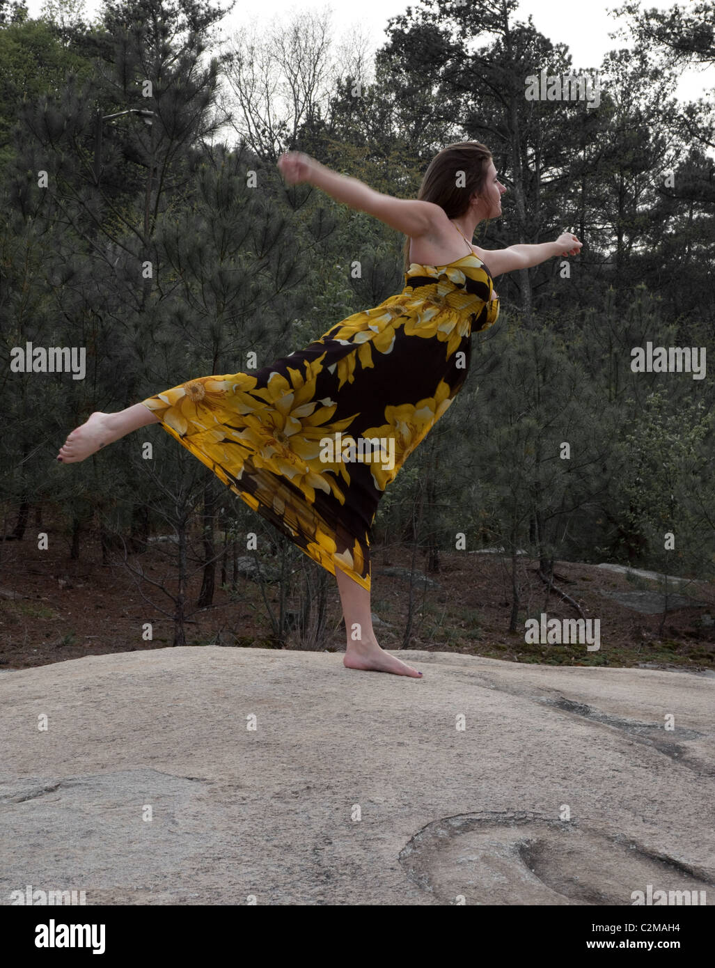 Pretty woman wearing a yellow dress, outside on a stone, dancing with ...