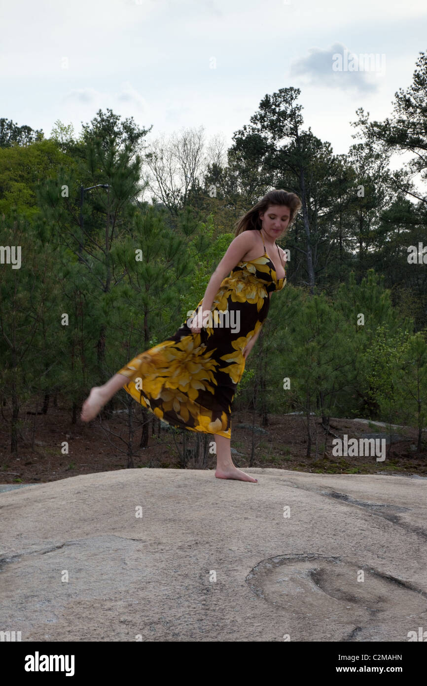 Pretty woman wearing a yellow dress, outside on a stone, dancing with ...