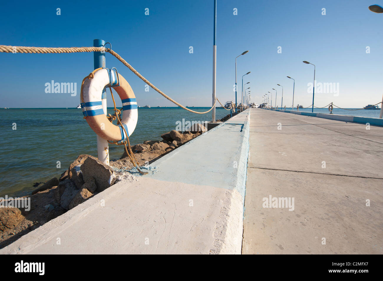 Long concrete jetty with boats moored and lifebuoy in foreground Stock ...