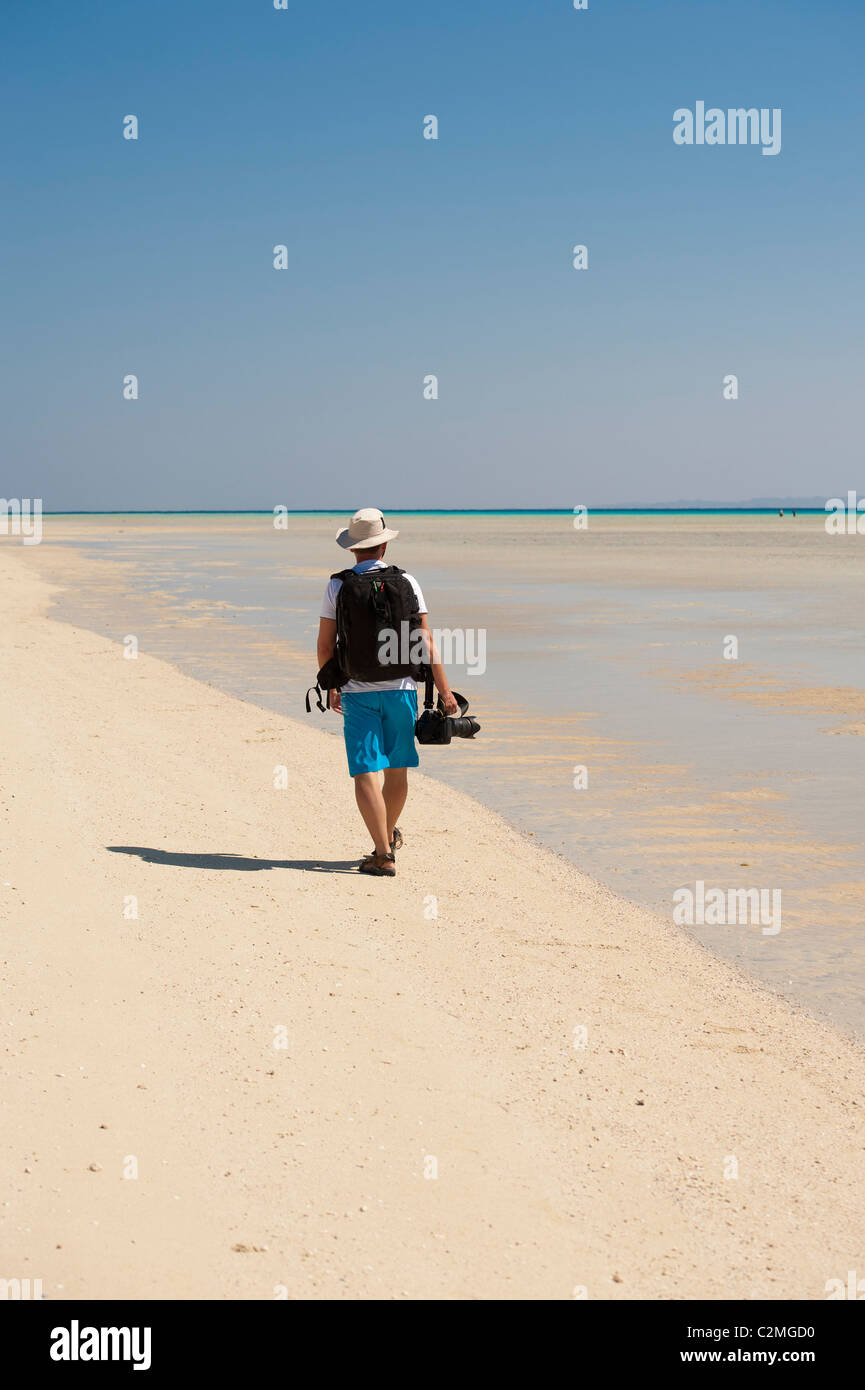 Photographer holding large slr camera walking along a tropical island ...