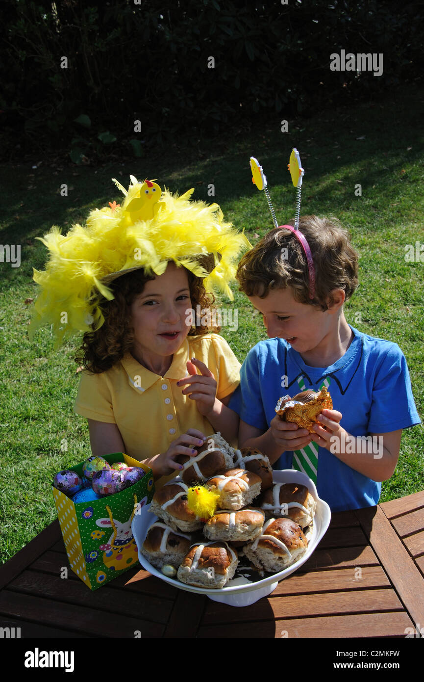 Boy and girl wearing Easter headgear and eating Hot cross buns and ...