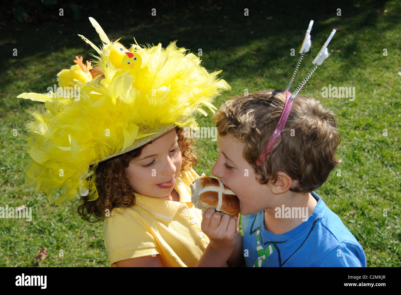 Boy and girl wearing Easter headgear and sharing a Hot Cross bun Stock ...