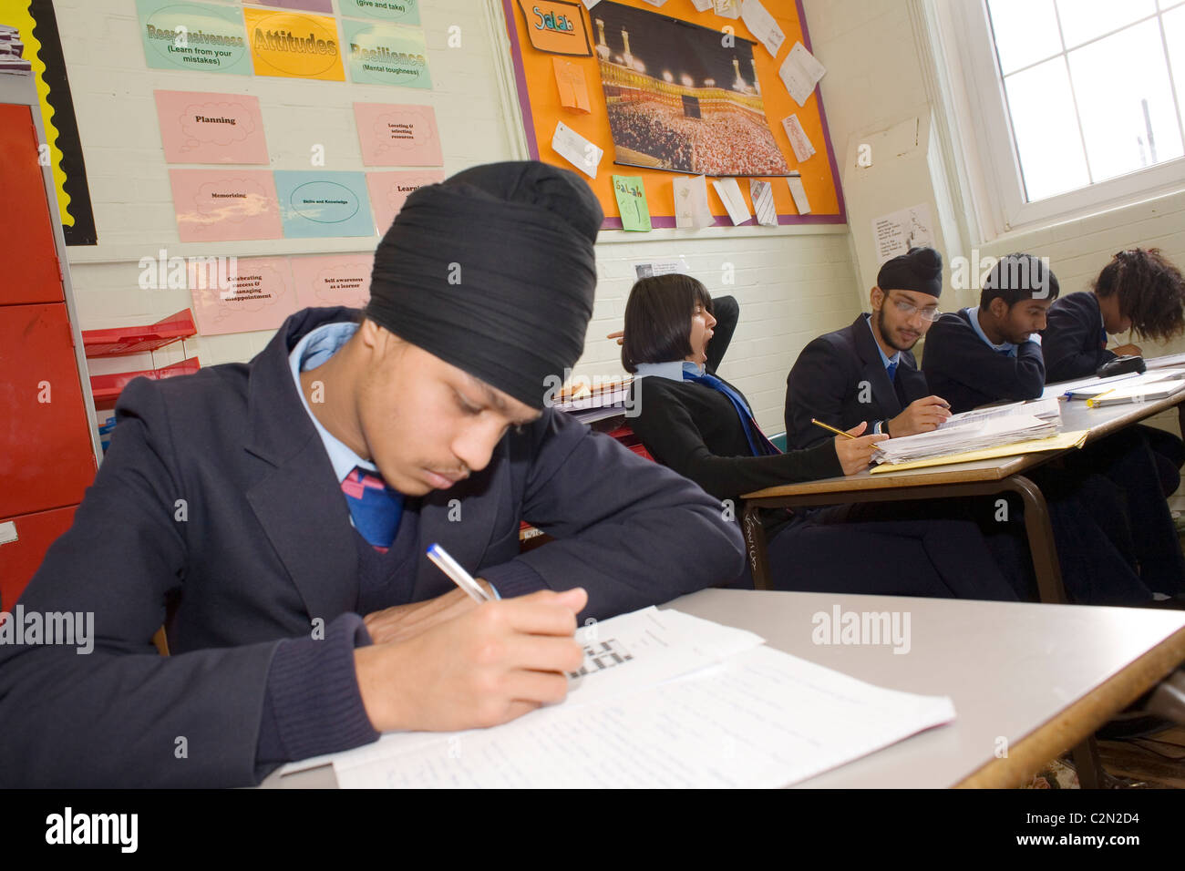 A Sikh boy in traditional head wear writes during a religious education ...