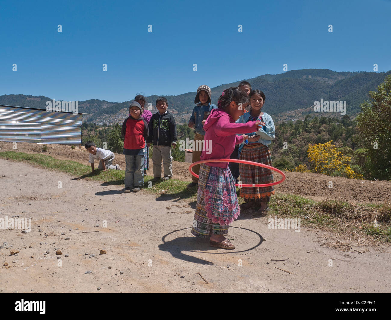Primary school kids take a break to play with a hula hoop along a dirt ...