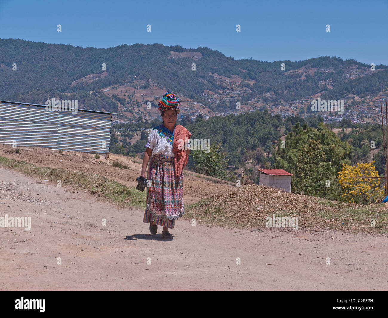 A Guatemalan woman walks along a dirt road midday carrying her load on ...