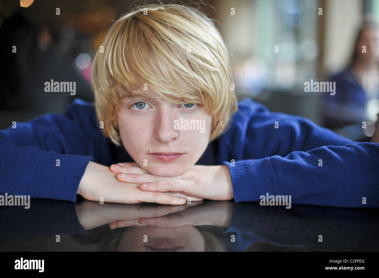Fair-haired teenage boy resting his head on his hands with in a ...