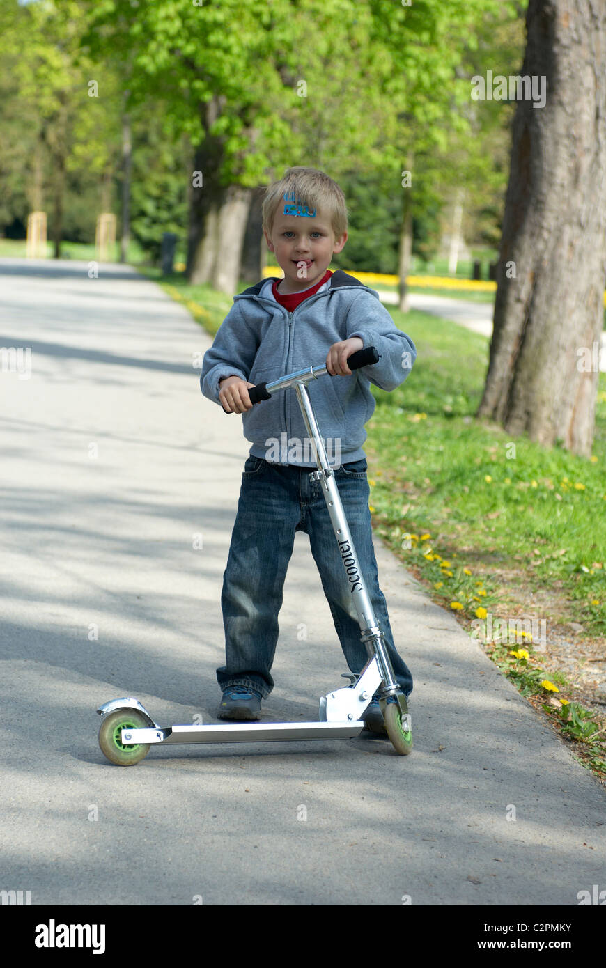 A young child blond boy on a scooter in park with injured head ...