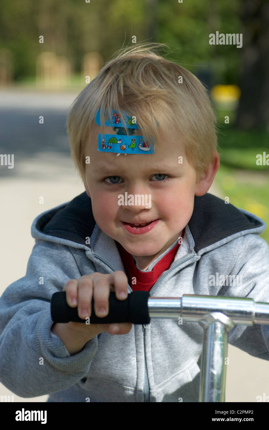 A young child blond boy on a scooter in park with injured head ...