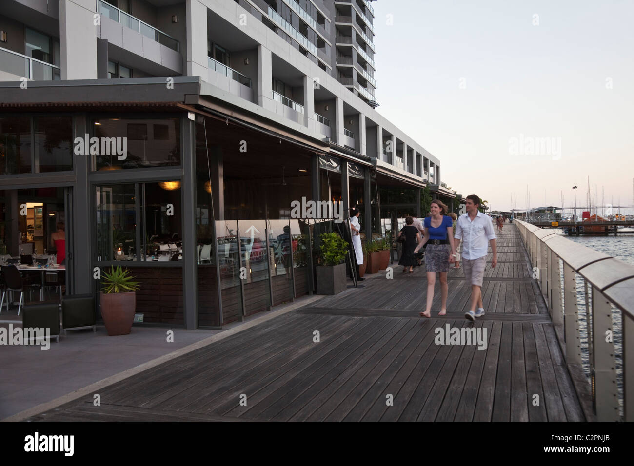 Couple walking along waterfront boardwalk at Harbour Lights. Cairns ...