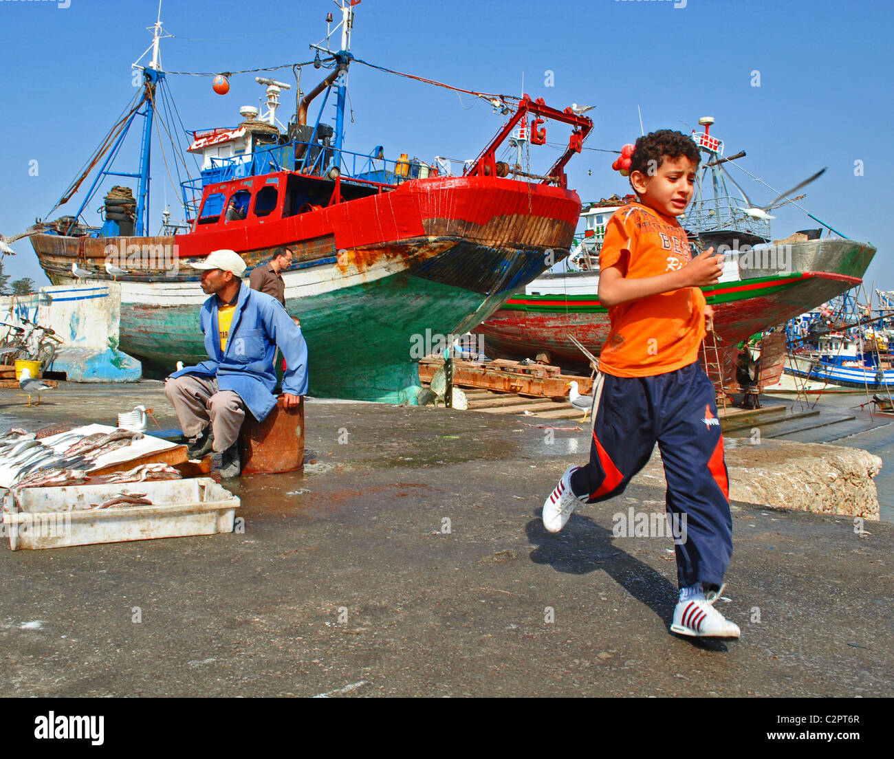 A child runs past fish vendors in the port in Essaouira, Morocco Stock ...