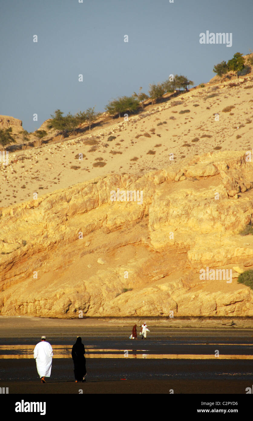 Oman, Sawadi, rear view of man and women in traditional dress walking ...