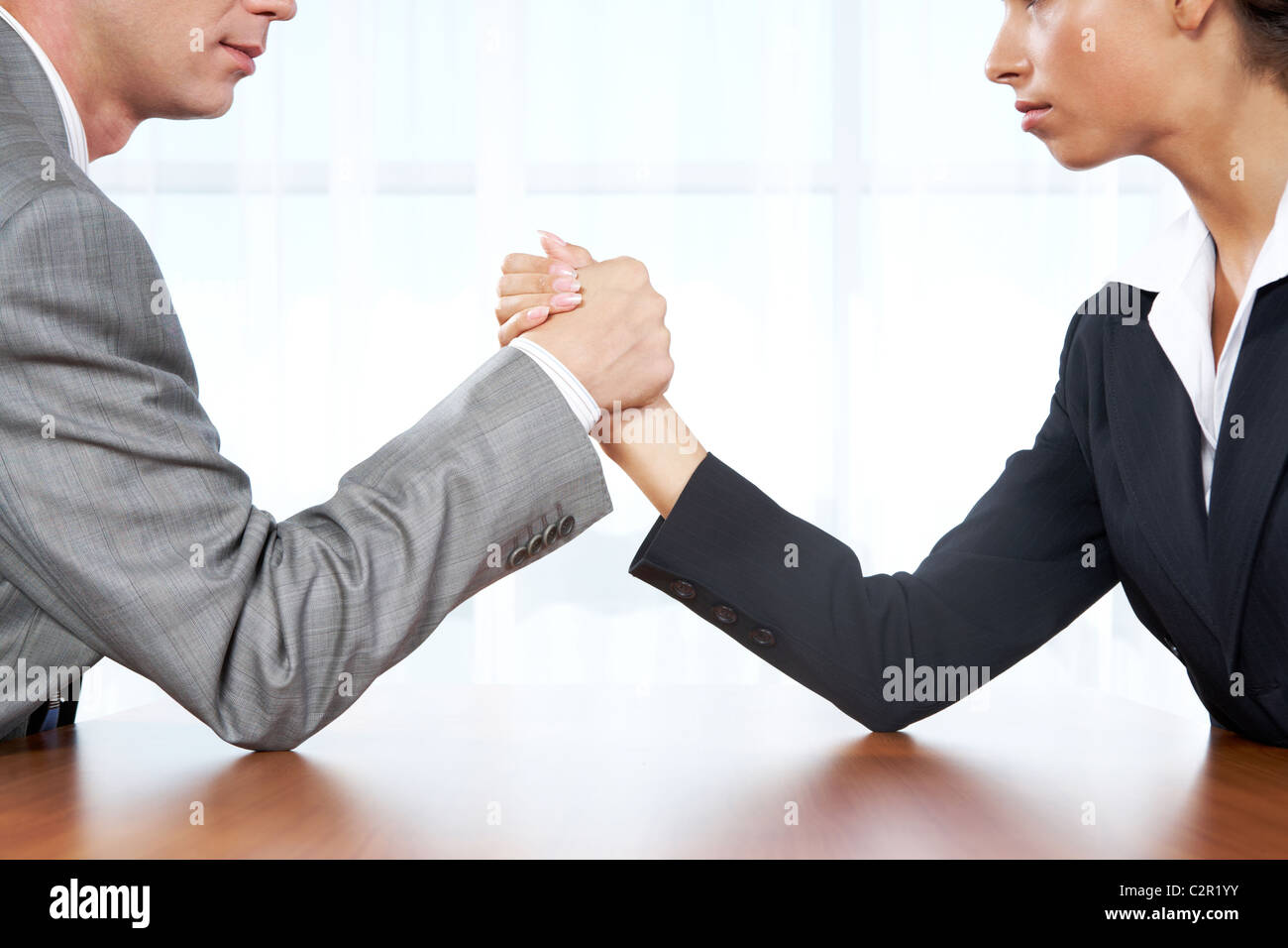 Portrait of business competitors doing arm wrestling and looking into ...