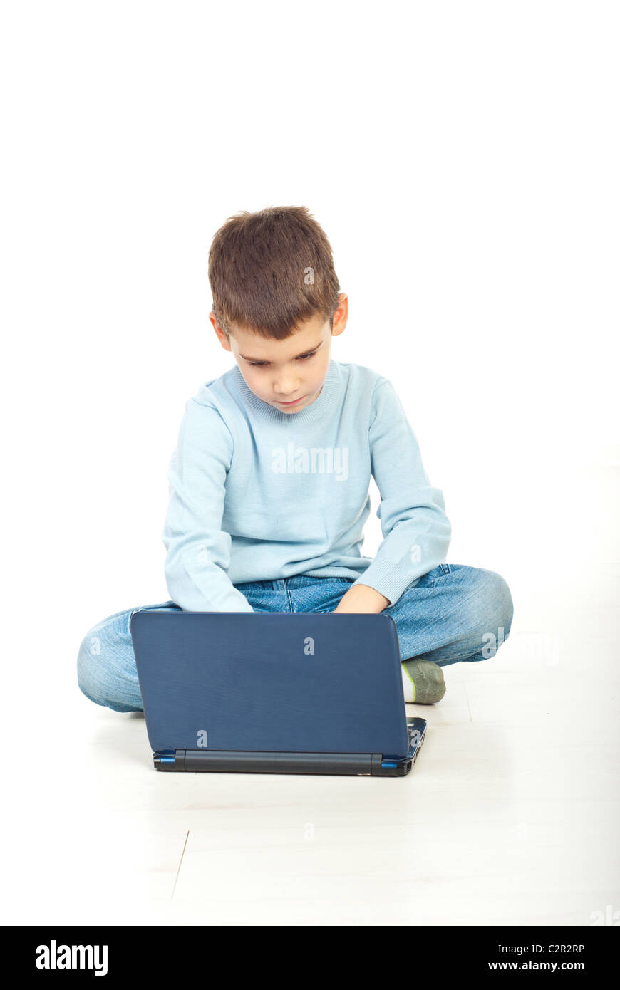 Preschool boy sitting with legs crossed on floor and using notebook ...