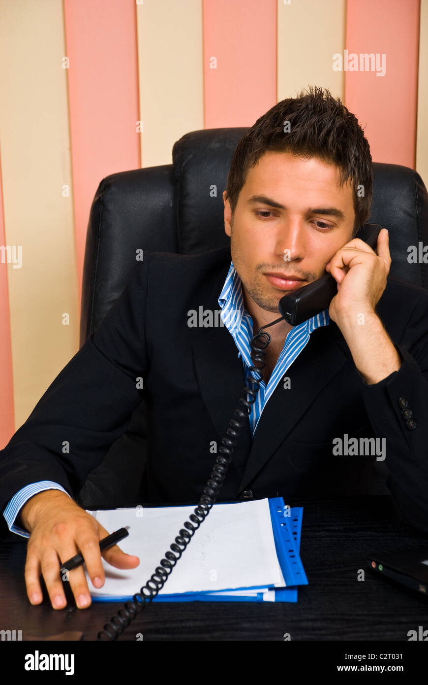 Sad business man sitting at desk in office talking at telephone and ...