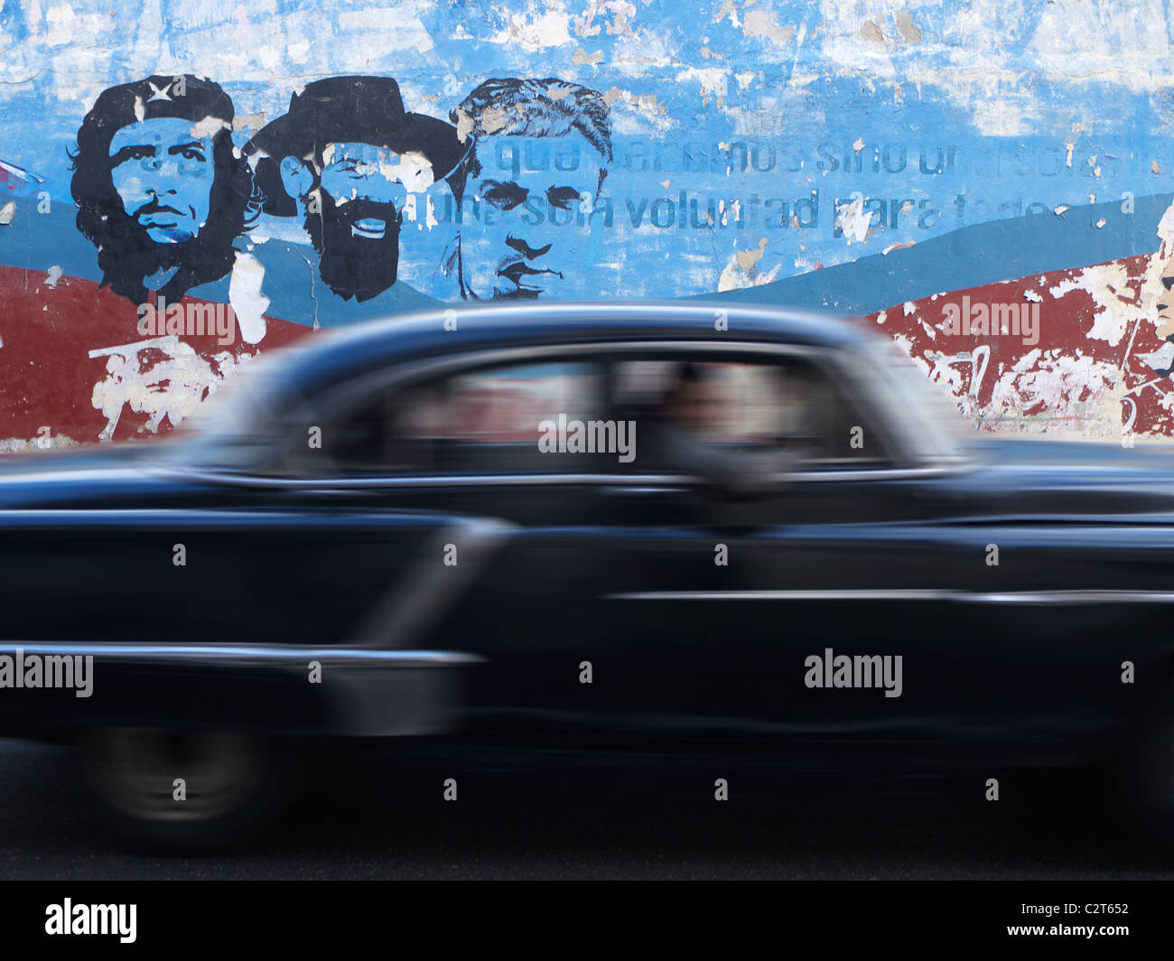 American classic car passing a wall painting of Che Guevara and Fidel ...