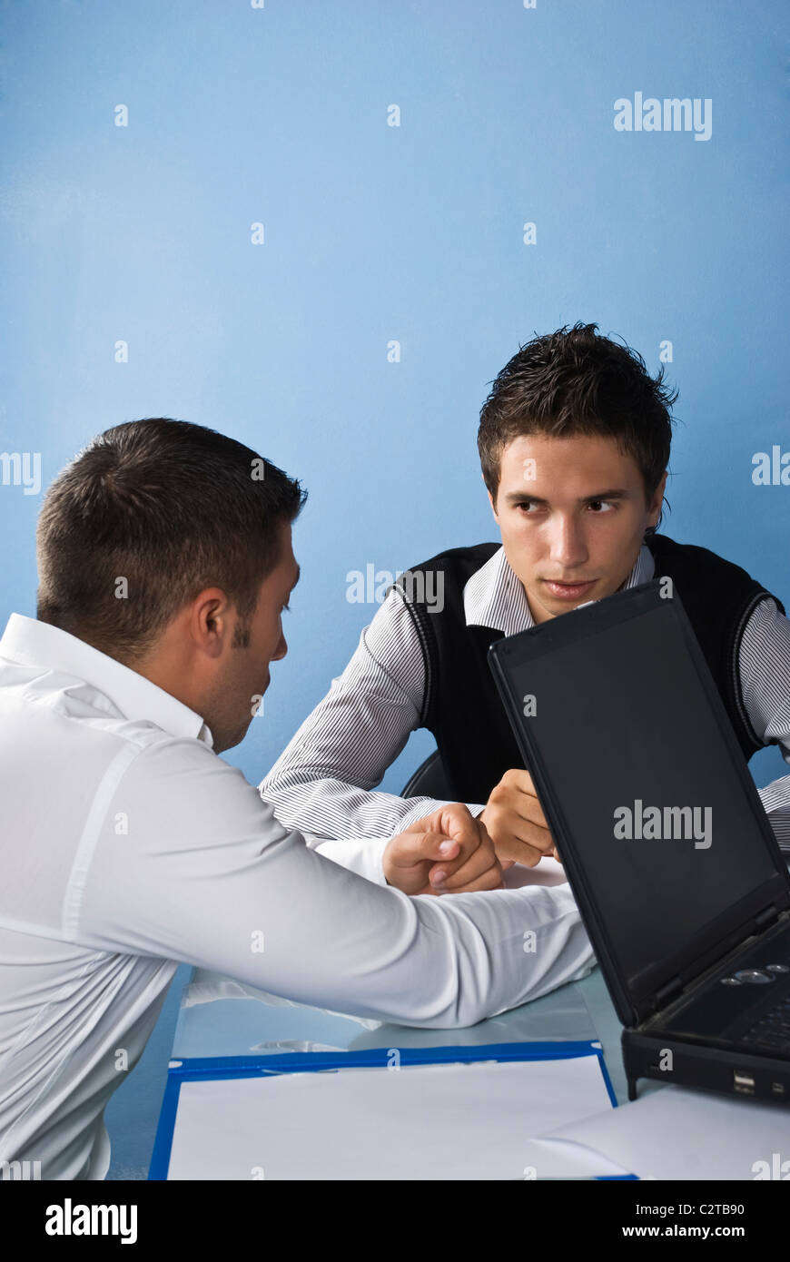 Two young business man having a secret conversation behind a laptop in ...