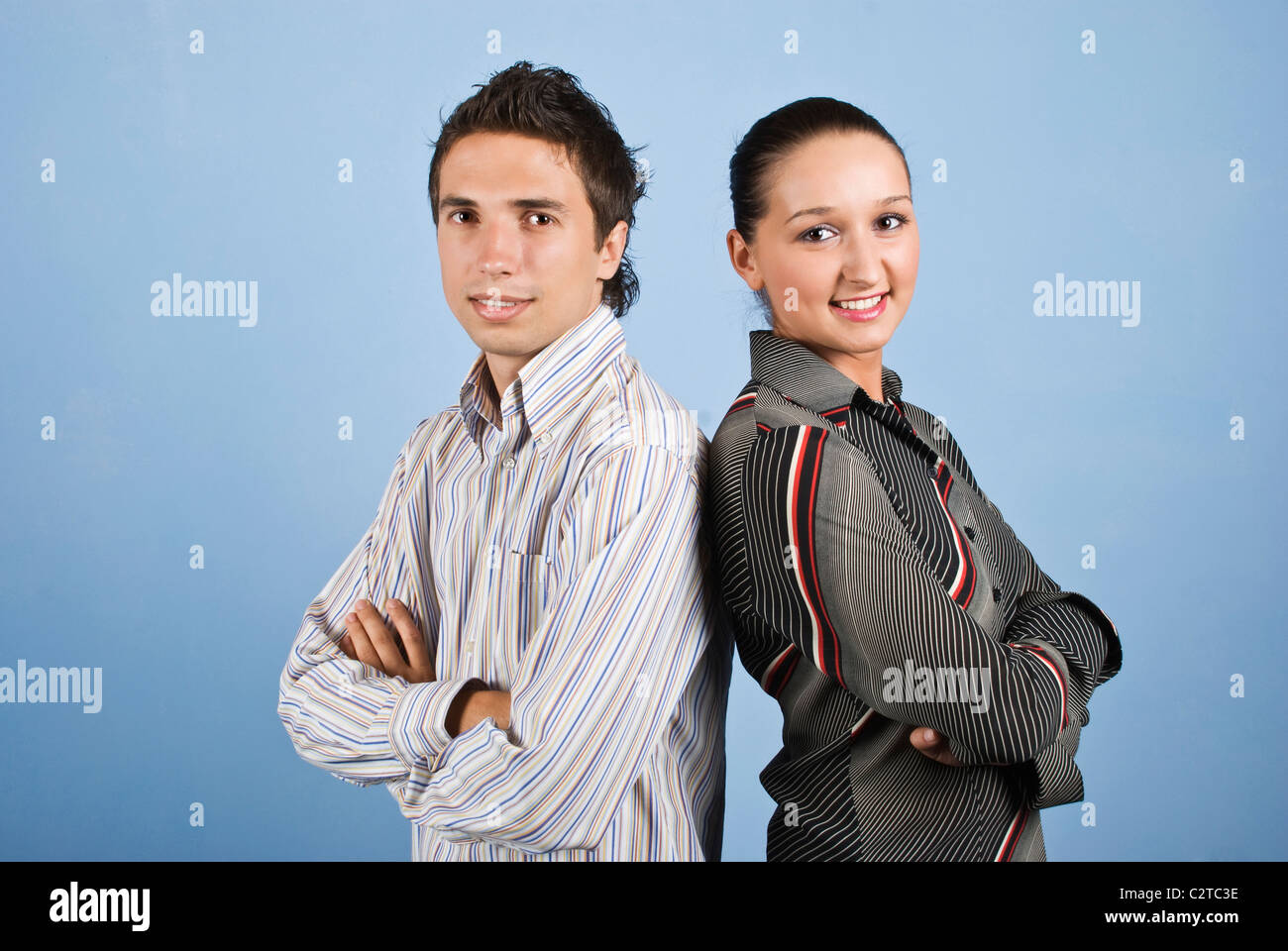 Young pair of business people standing back to back with arms crossed ...