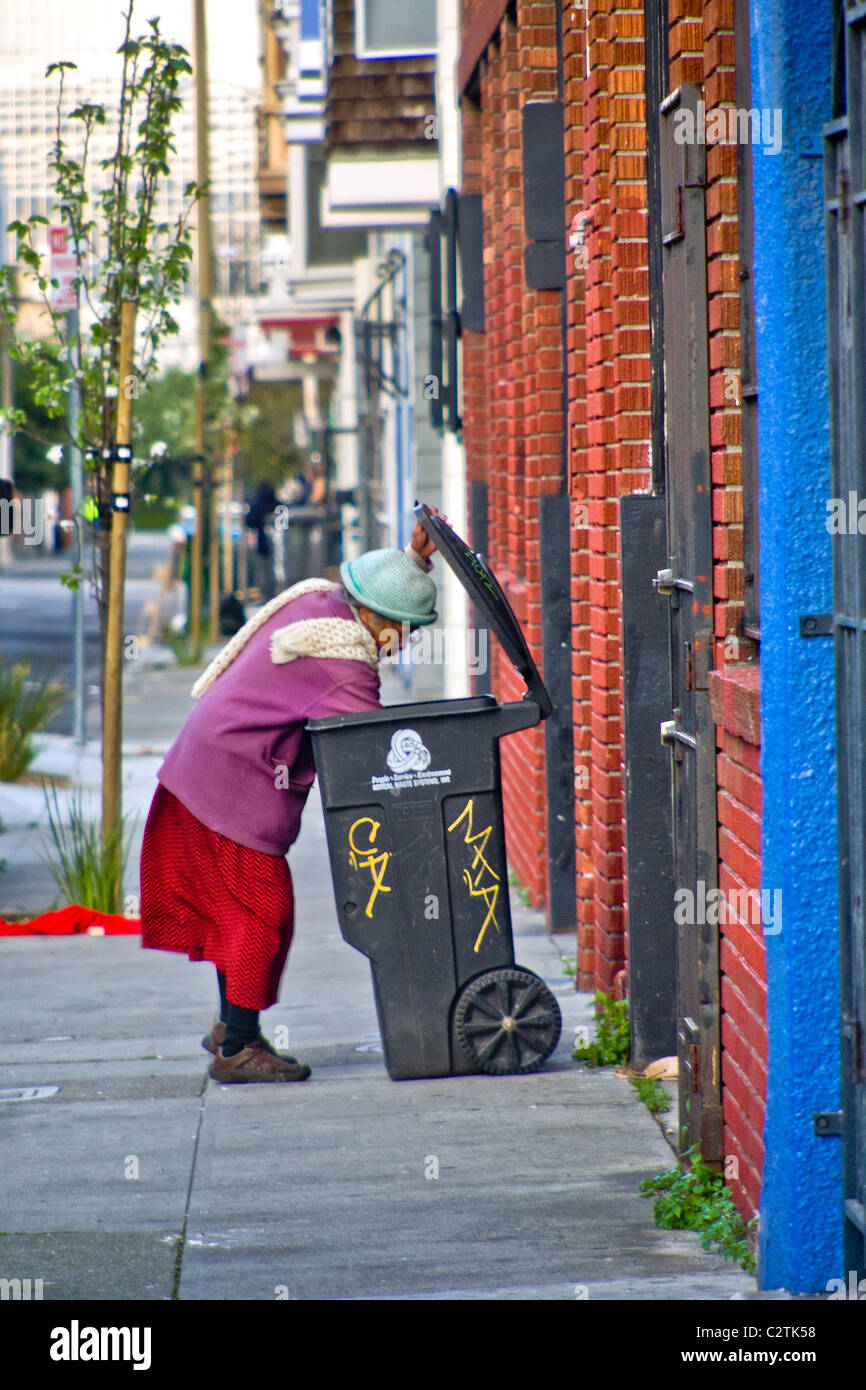 A homeless African American woman searches a garbage can for food on ...