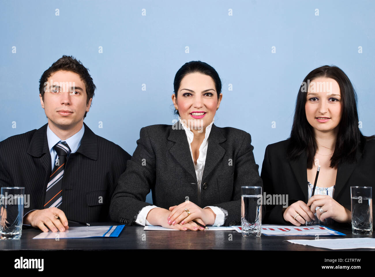 Three business people sitting in a line at table at conference and they ...