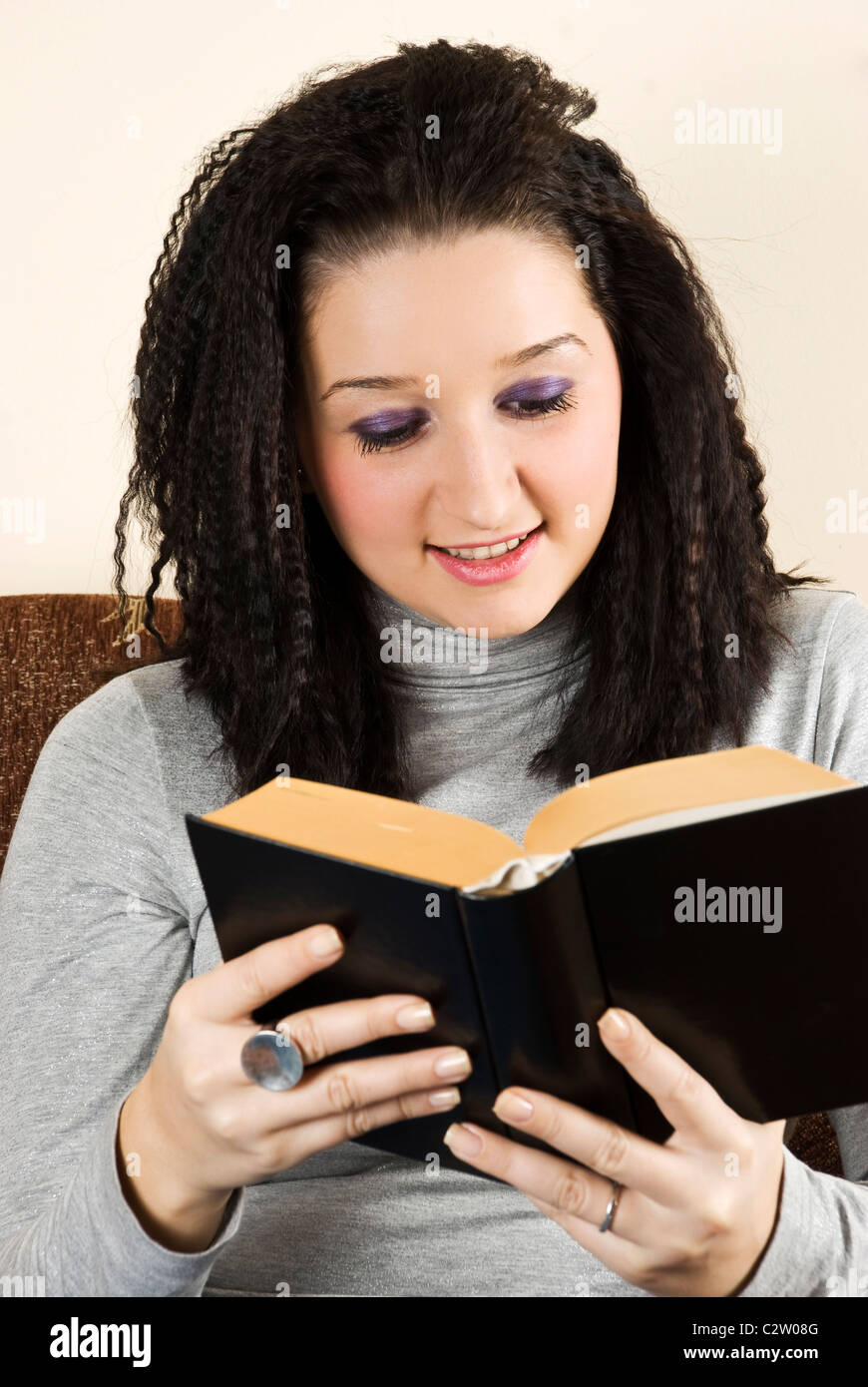 Teen female read a book and smiling in a sofa Stock Photo - Alamy