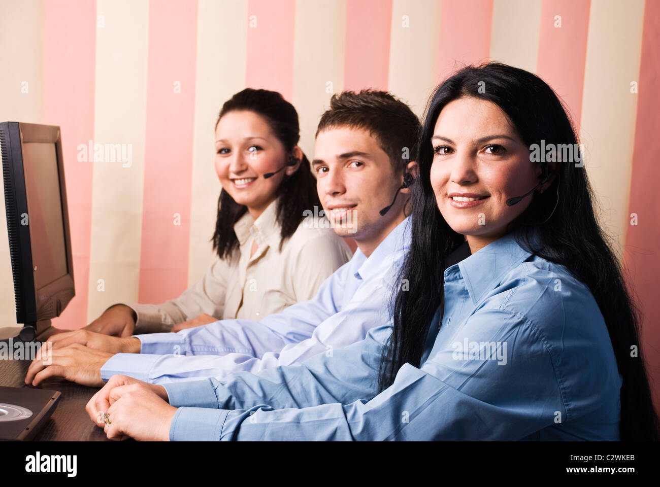 Three business people support operators working on computers in office ...