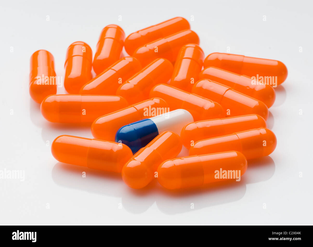 orange colored pills on white background surrounding a different pill ...