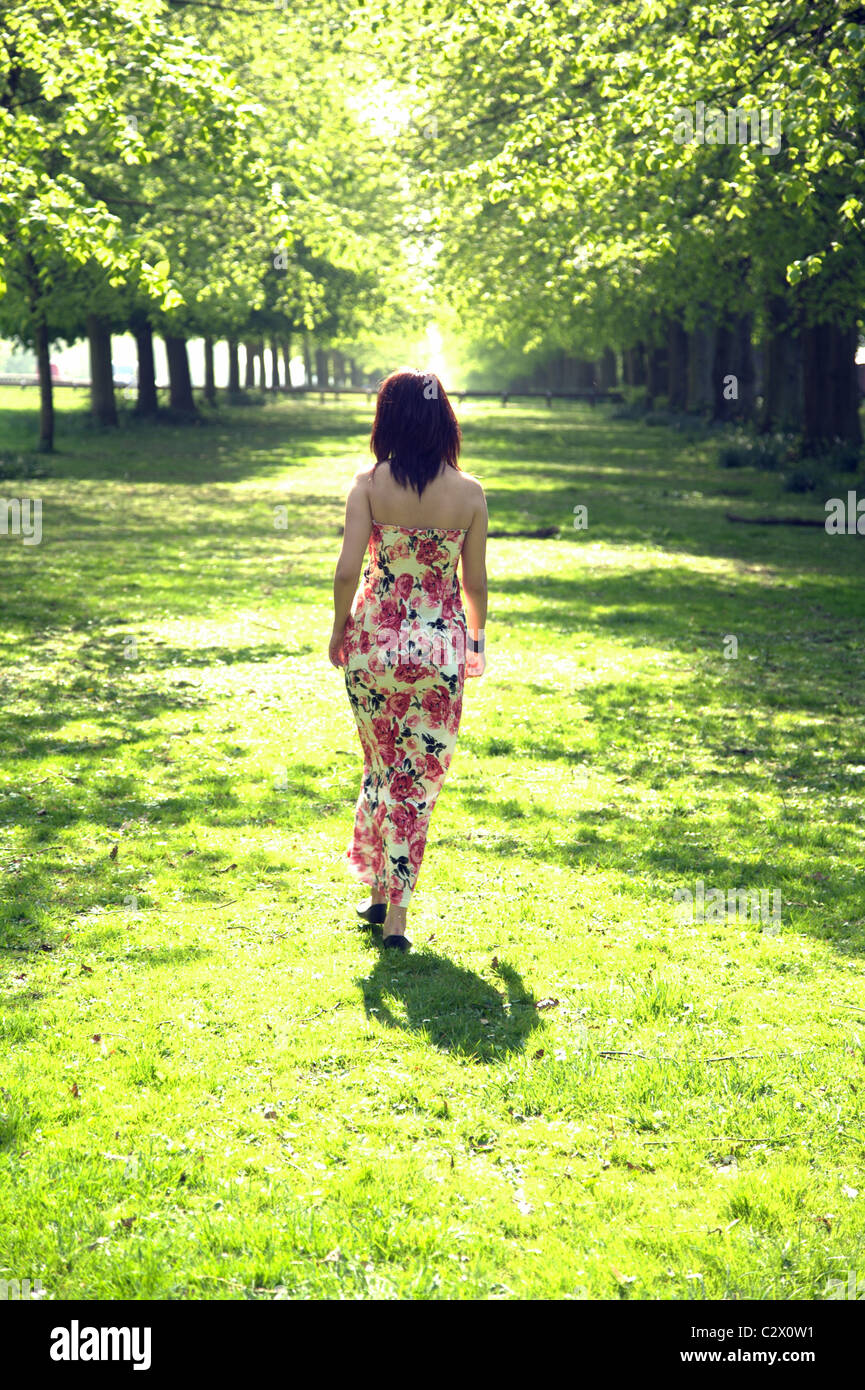 woman in a floral dress walking down a treelined pathway Stock Photo ...