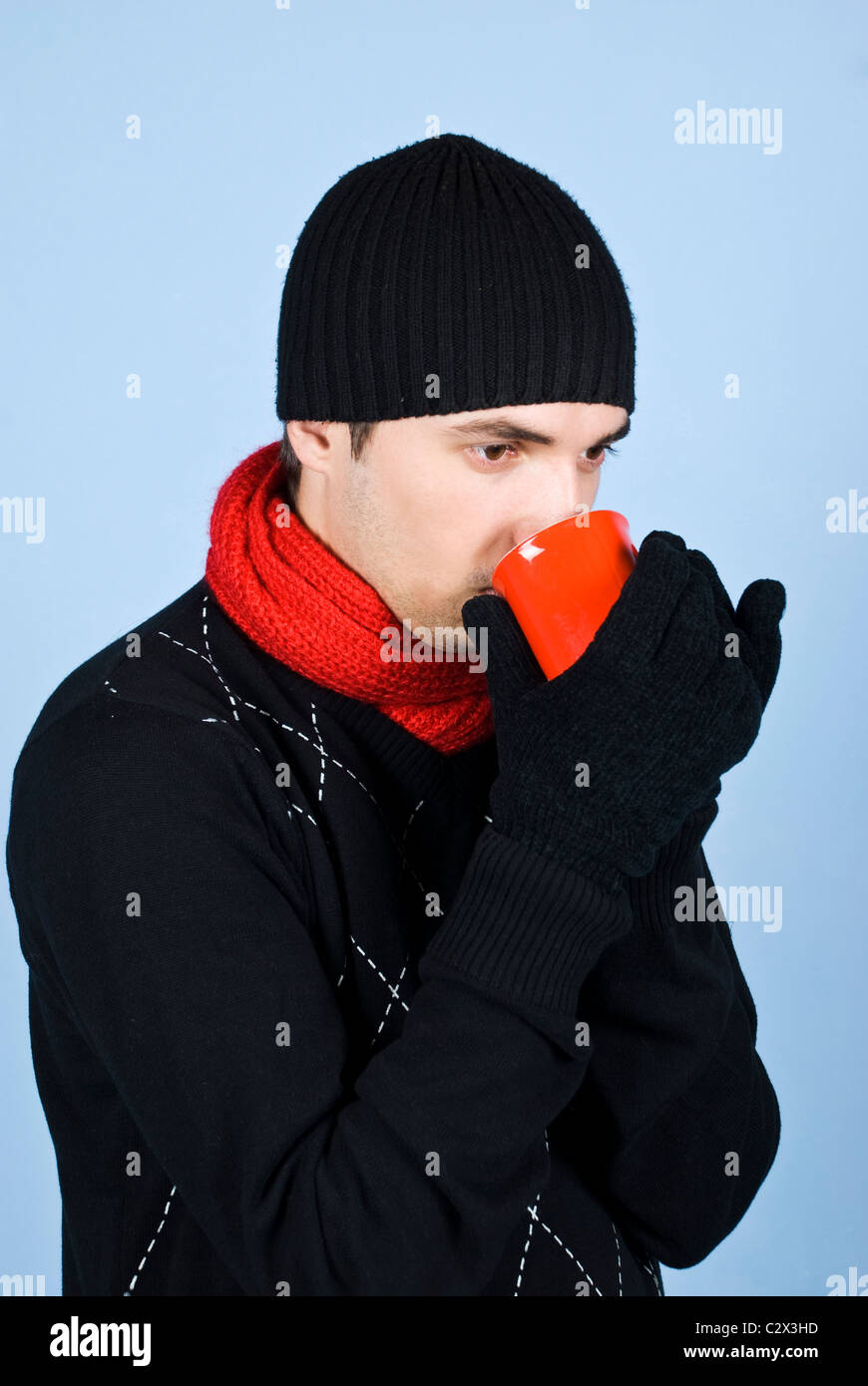 Young man standing in profile and drinking hot tea from a red mug,he ...